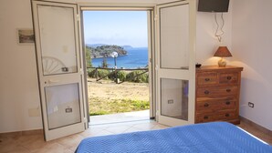 Quarto com cama, cômoda, televisão e vista para o mar.