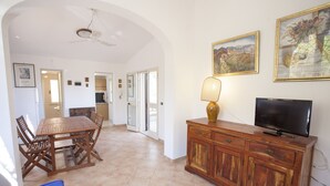 Uma sala de estar ampla com uma mesa de jantar, cadeiras, uma TV em um móvel de madeira e obras de arte nas paredes.