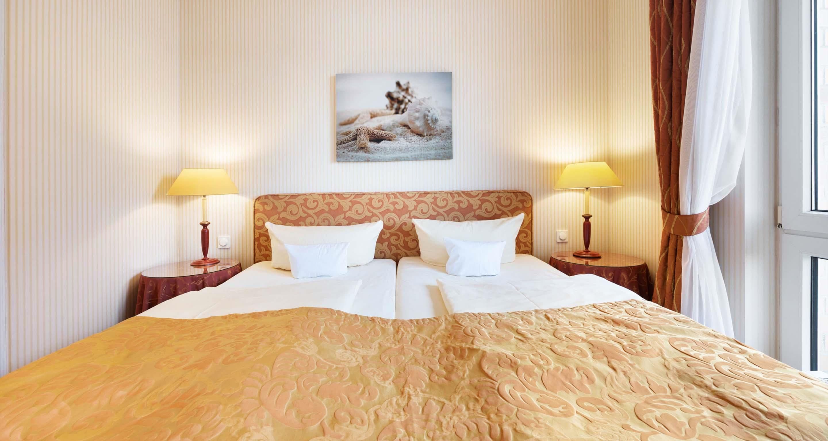 Quarto de hotel com uma cama grande, duas luminárias de cabeceira, um painel decorativo e um quadro na parede.
