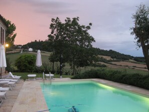 Piscina com espreguiçadeiras e guarda-sóis, cercada por vegetação e colinas ao fundo.