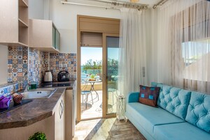 Cozinha moderna com painel de azulejos, forno embutido e pia. Há uma porta de vidro deslizante que dá para um espaço de pátio externo com mesa e cadeiras. Um sofá azul está posicionado perto da porta.