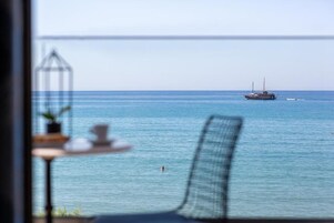 Vista do mar a partir de uma varanda com mesa e cadeira, um navio ao longe e céu claro.