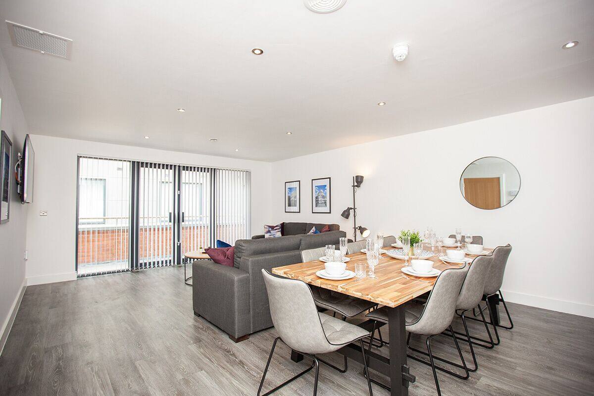 Uma sala de jantar moderna com uma mesa de madeira posta para quatro pessoas, cadeiras estofadas cinzas e um sofá cinza.