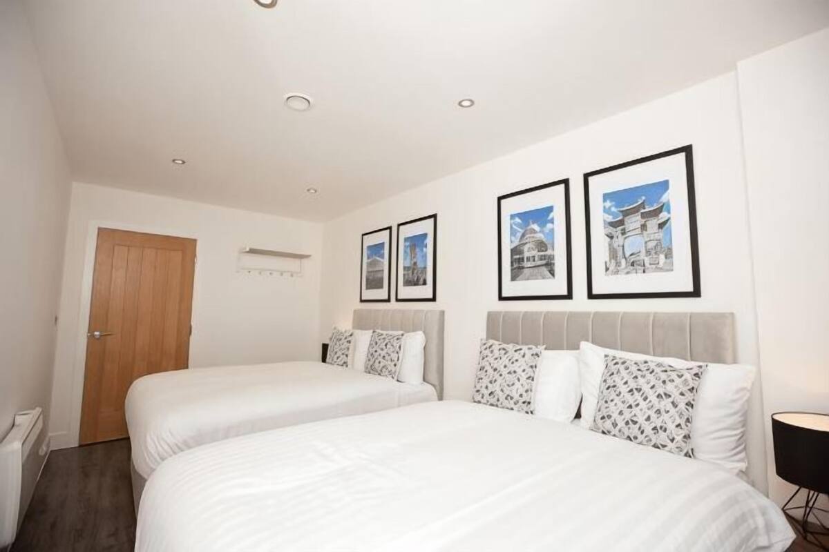Quarto de hotel com duas camas, porta de madeira e quadros nas paredes.