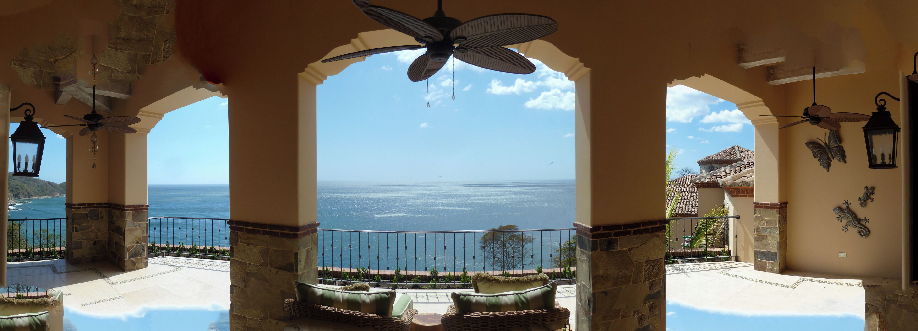 Uma varanda com vista para o oceano, pilares de pedra e ventiladores de teto.