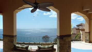 Uma varanda com vista para o oceano, pilares de pedra e ventiladores de teto.