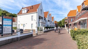 Rua de paralelepípedos com edifícios de estilo europeu tradicional, uma placa com texto e um ciclista ao longe.