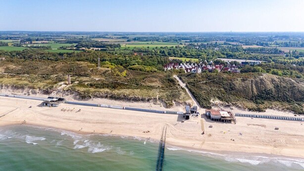 Vista aérea de uma área costeira com praia, uma ponte e um conjunto de edifícios.
