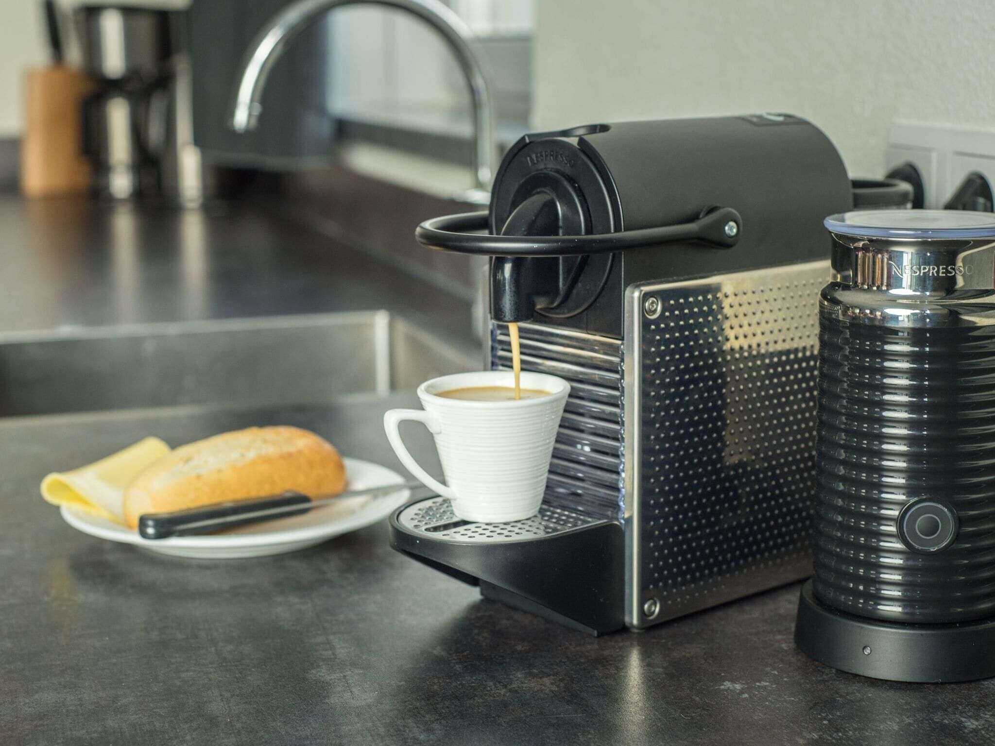 Uma máquina de café com uma chávena de café e um croissant numa bancada de cozinha.