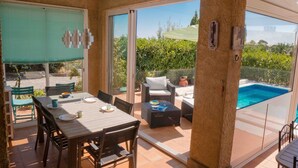 Um pátio externo com mesa e cadeiras, uma piscina e vista para o verde.