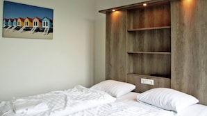 Quarto com duas camas, uma estante de madeira e um quadro com casas de praia.