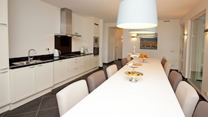 Uma cozinha moderna com armários brancos, bancada preta e um espaço de refeições com mesa e cadeiras brancas.