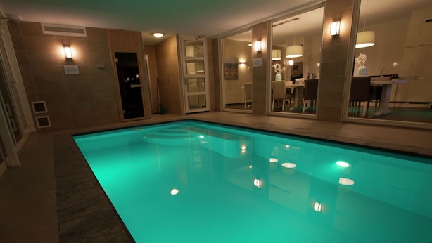 Uma piscina com água cristalina, rodeada por um espaço com azulejos e uma porta de vidro que dá para um quarto.