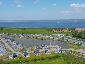 Zona residencial à beira-mar com casas modernas, um lago central e vista para o mar com veleiros.