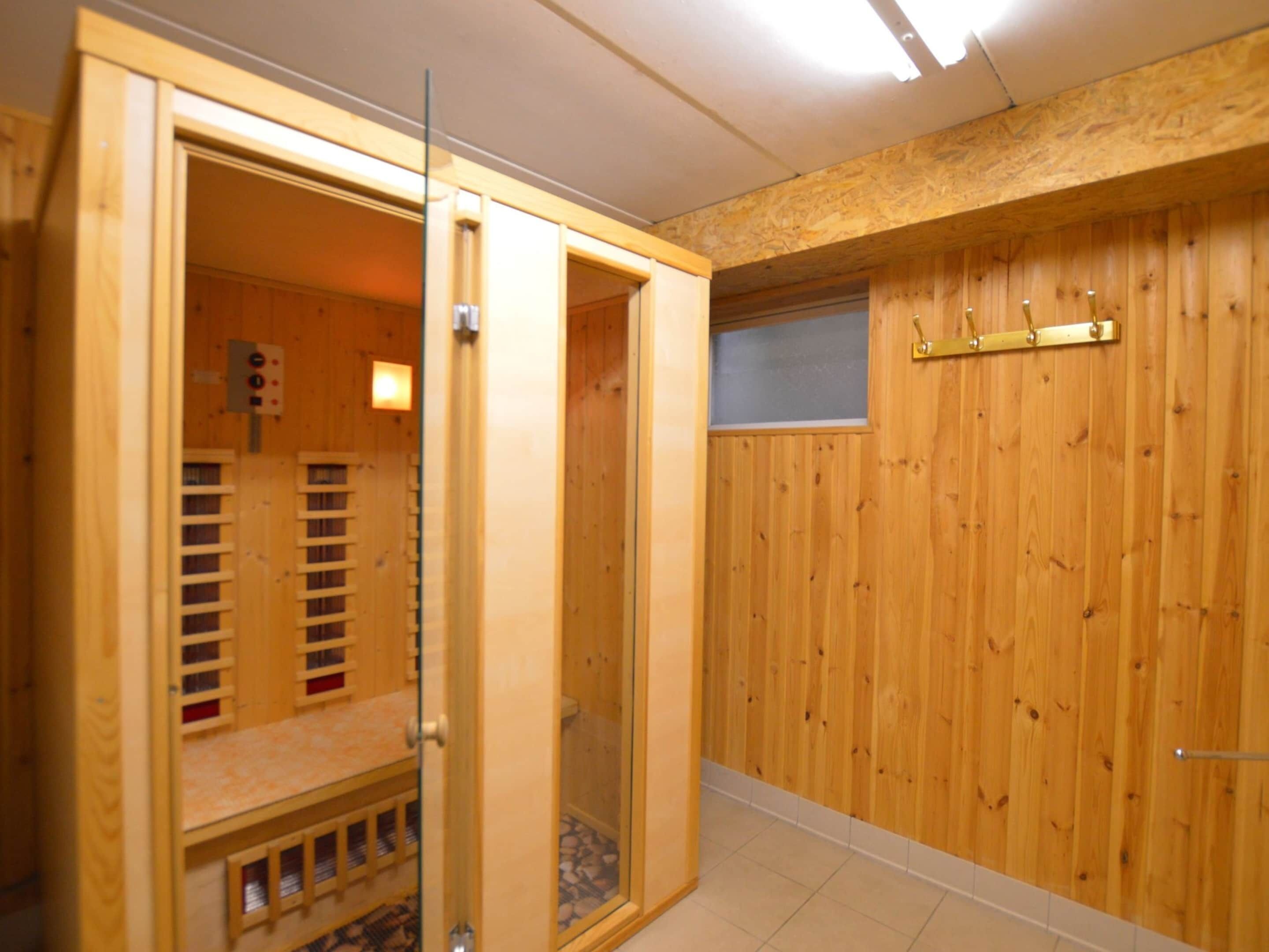 Uma sala de sauna com paredes de madeira e porta de vidro, um banco de madeira e um porta-toalhas.