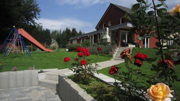 Uma casa residencial com um jardim da frente, um escorrega e um jardim de rosas.