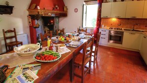 Uma cozinha com uma mesa de jantar posta para refeição, uma chaminé vermelha e uma janela com cortinas.