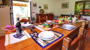Uma sala de jantar com mesa de madeira posta para refeição, rodeada por cadeiras.