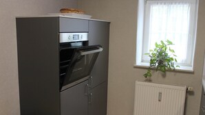 Uma cozinha compacta com forno embutido, um refrigerador pequeno e uma janela com uma planta.