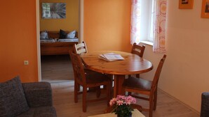 Uma sala de jantar com mesa e cadeiras de madeira, um sofá e uma pequena mesa com flores.