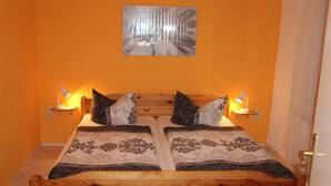 Uma cama de casal com estrutura de madeira, duas luminárias de cabeceira e um cobreleite estampado.
