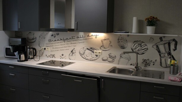 Cozinha moderna com armários escuros, bancada branca e backsplash com ilustrações de alimentos e o texto "Breakfast all day".