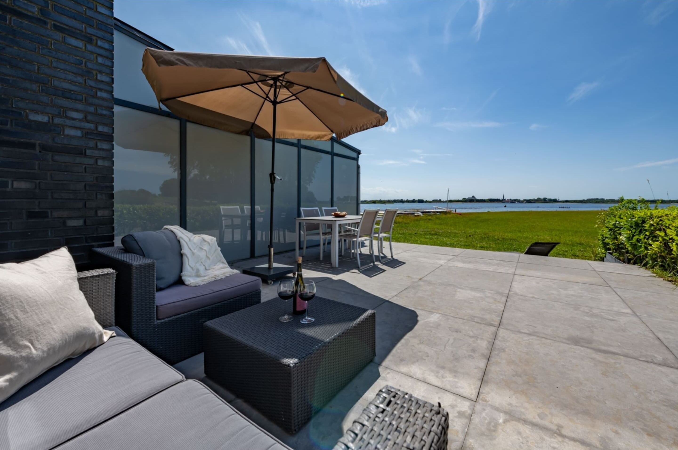 Um terraço ao ar livre com estrutura de vidro, mobiliário e vista para a água.