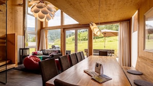 Um quarto espaçoso com uma grande mesa de jantar de madeira, assentos confortáveis e amplas janelas com vista para uma paisagem verde.