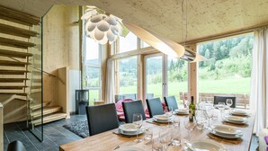 Uma área de jantar com uma mesa de madeira posta para seis pessoas, grandes janelas e vista para o exterior.