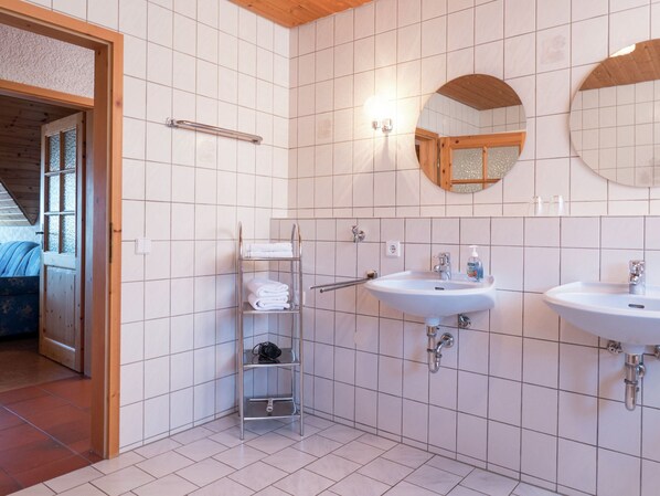Casa de banho com paredes revestidas de azulejos brancos, duas pias, um espelho e um porta-toalhas.