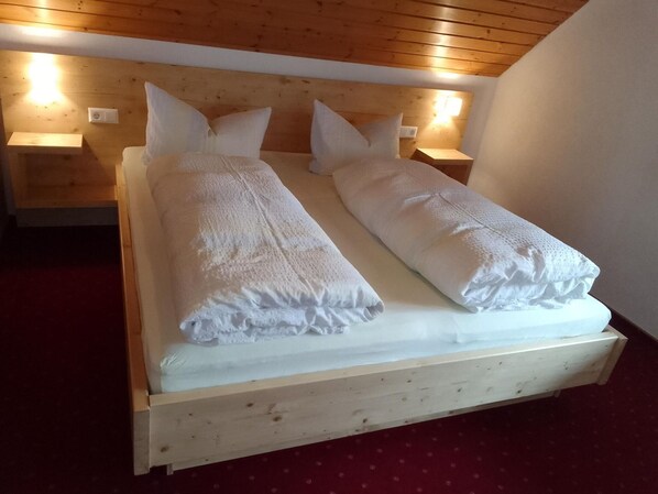 Uma cama beliche de madeira com duas almofadas e um cobertor, equipada com luzes de leitura fixadas na parede.