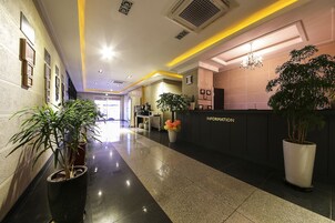 Uma área de recepção de hotel com balcão, relógio e planta em vaso.