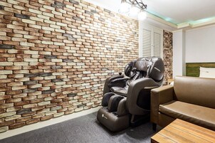 Uma cadeira de massagem em um quarto com parede de tijolos e uma mesa de madeira.