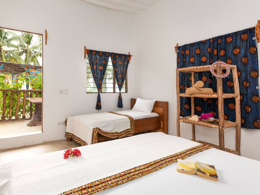 Quarto com cama, janela com cortinas, prateleira de madeira com um urso de pelúcia e vista para palmeiras.