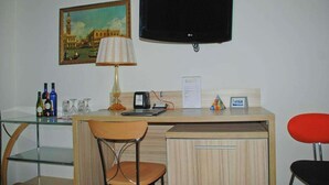 Quarto de hotel com uma escrivaninha, televisão, luminária, cadeira e uma pequena mesa com garrafas e copos.