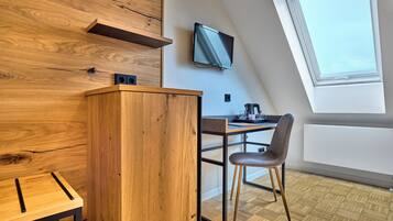 Quarto moderno com parede de destaque em madeira, uma escrivaninha com cadeira, televisão montada e uma janela grande.