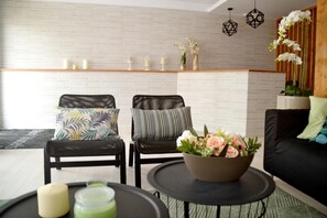 Uma sala de estar moderna com duas cadeiras pretas, um sofá preto, uma mesa de centro redonda com um arranjo floral e uma parede com padrão de tijolos.