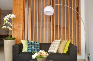 Sala de estar moderna com sofá preto, almofadas estampadas, luminária pendente branca e divisória de madeira ripa.