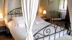 Quarto com cama de dossel, mesa de cabeceira com luminária, cadeira e radiador.