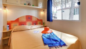 Quarto de hotel com uma cama, janela com vista para árvores, mesa de cabeceira e um armário com objetos.