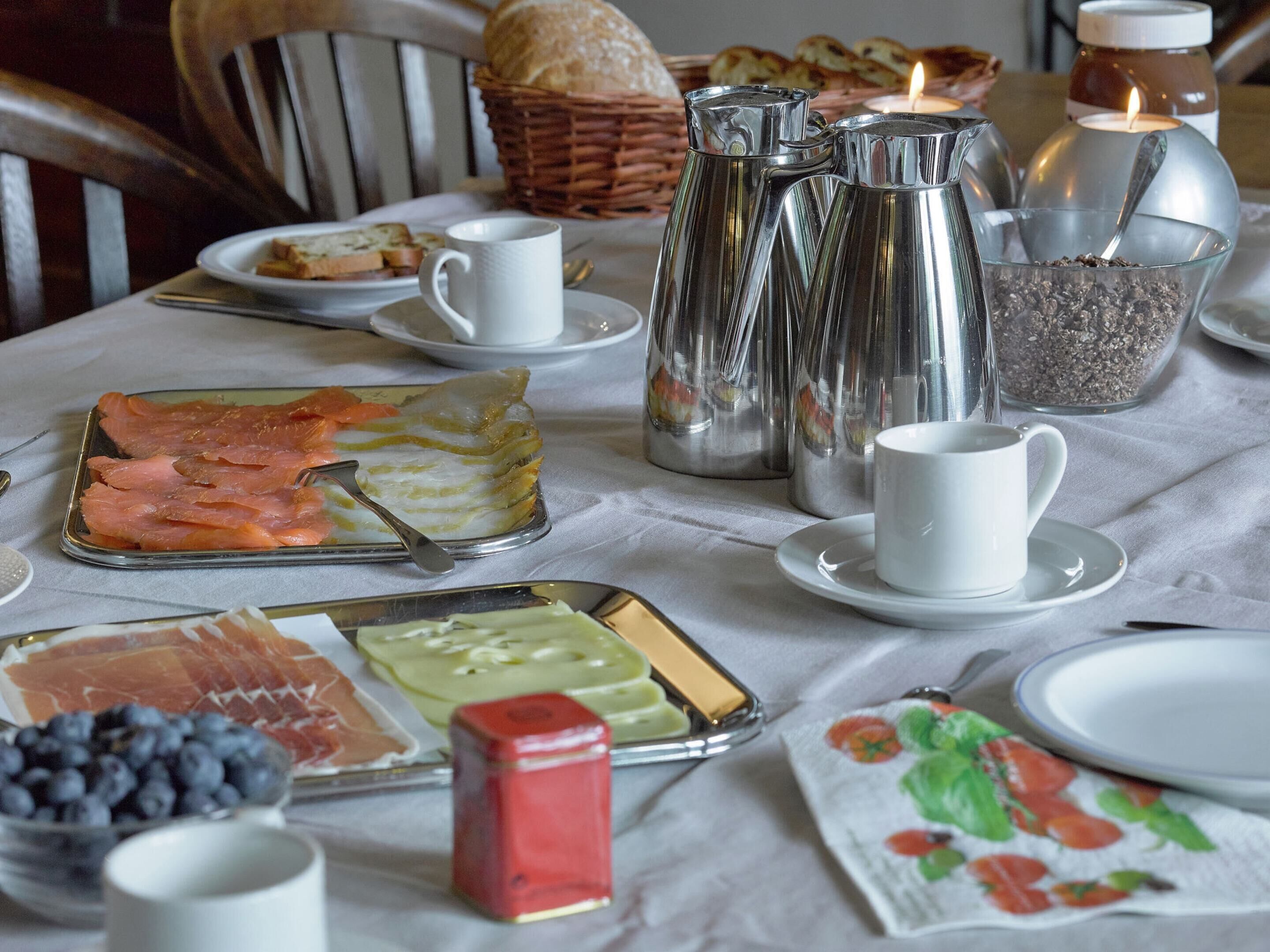 Uma mesa de café da manhã com diversos alimentos, incluindo salmão defumado, queijo e uma cesta de frutas.