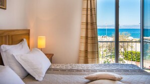 Quarto de hotel com cama, mesa de cabeceira, abajur e vista para o mar através de uma varanda.