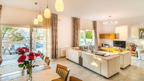 Cozinha moderna com ilha central, área de jantar com mesa e cadeiras, e sala de estar com sofá e televisão.
