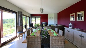 Uma sala de jantar com móveis de vime, uma mesa comprida posta para quatro pessoas e uma televisão ao fundo.
