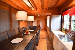Interior em madeira com mesa de jantar, cadeiras, cozinha com pia e geladeira.