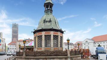 Uma torre histórica com relógio, rodeada por ruas de paralelepípedos e edifícios tradicionais.
