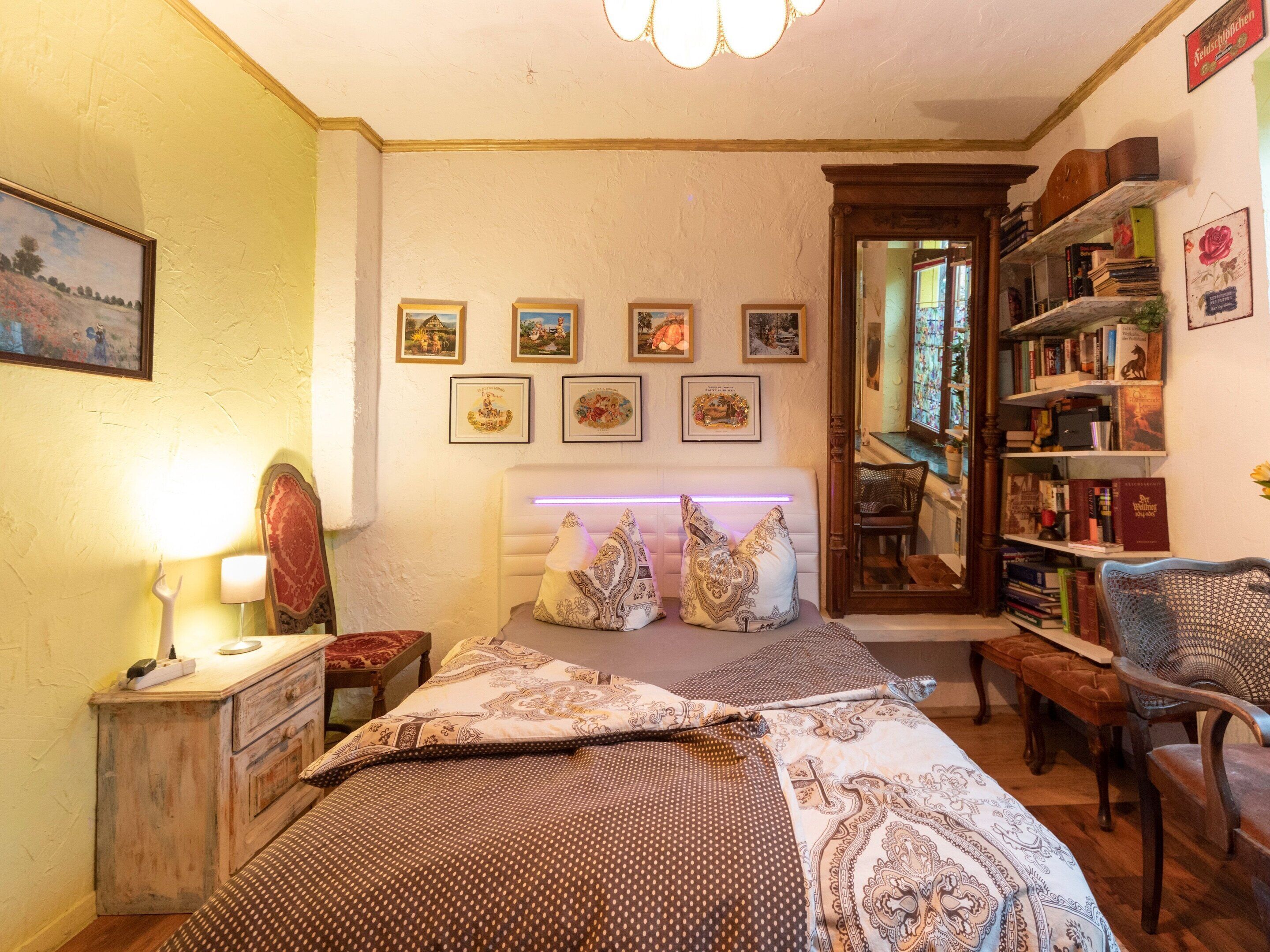 Um quarto aconchegante com cama, mesa de cabeceira, luminária e estante.