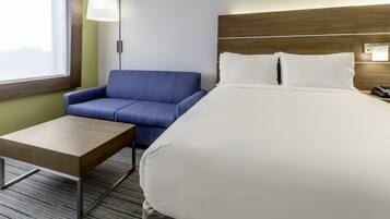 Quarto de hotel com cama, sofá azul, mesa de madeira e luminária.