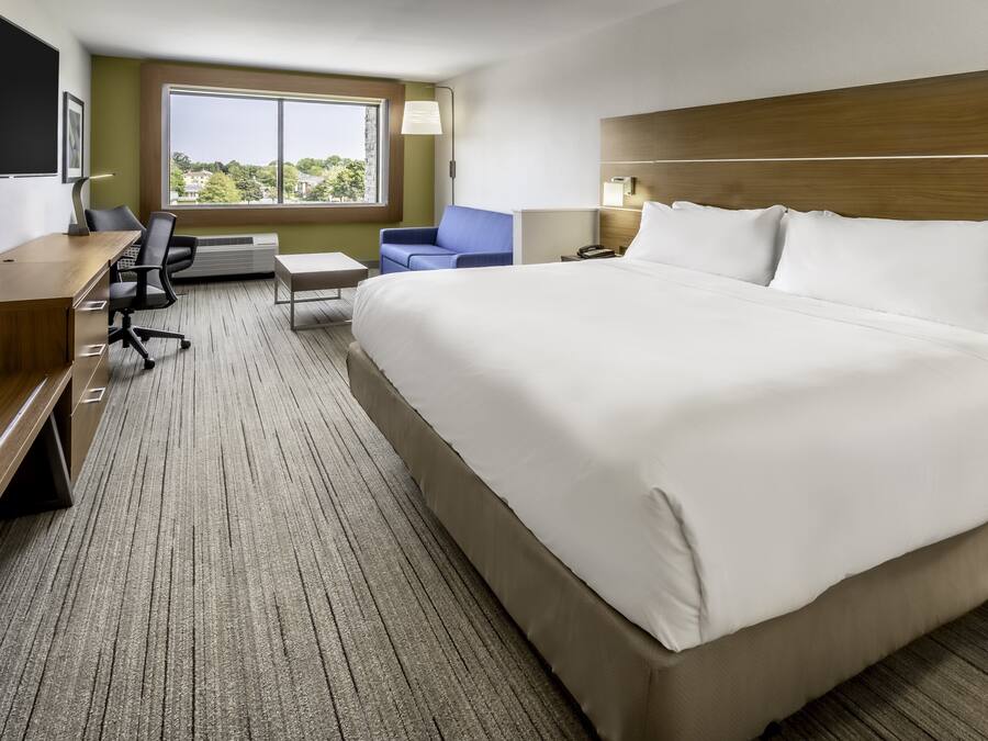Quarto de hotel com uma cama grande, uma escrivaninha com cadeira, uma mesinha e uma janela com vista para o verde.