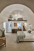 Um quarto amplo tipo loft, com teto alto, uma cama grande, uma escrivaninha e escada para um andar superior.